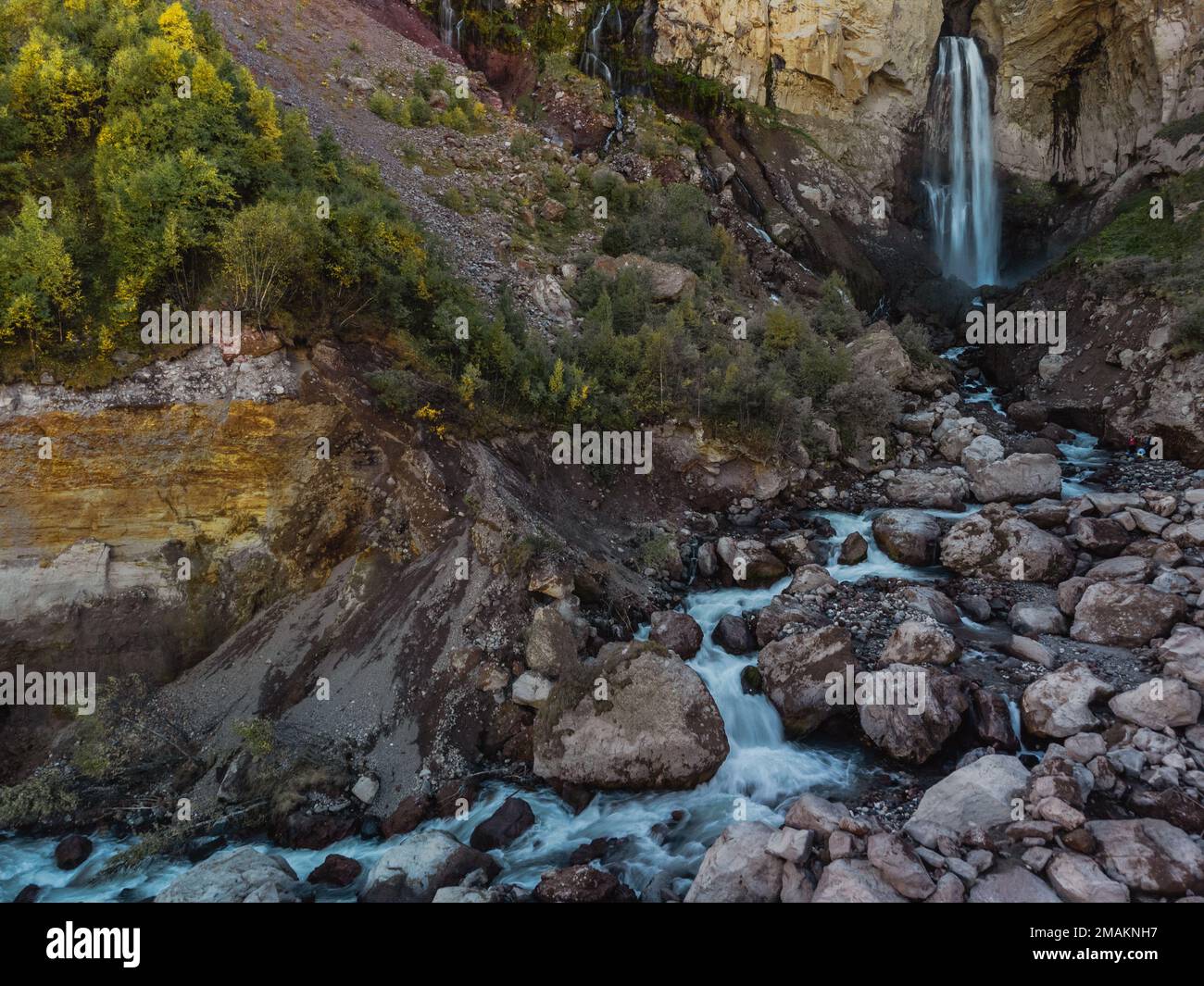A smooth stream of water flows down from a cave in the high rocks of ...