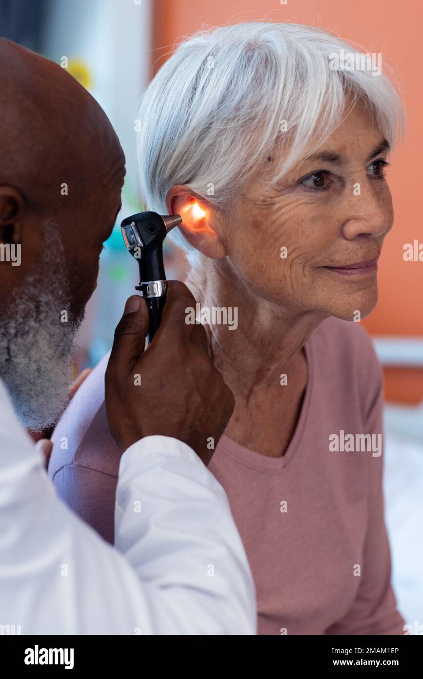 Vertical of diverse senior male doctor using otoscope on ear of senior ...