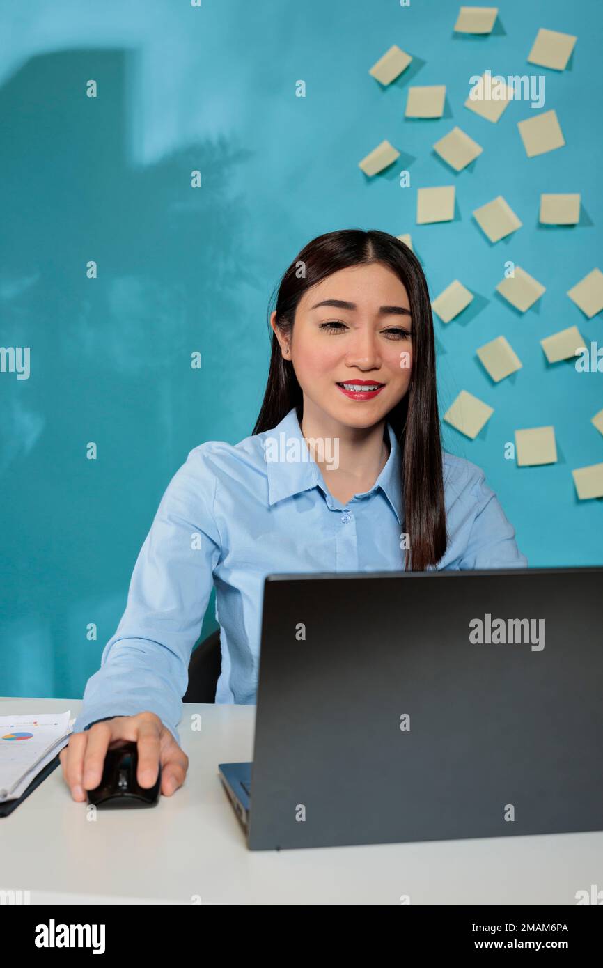 Asian woman working on a laptop computer in a modern office doing business research in a startup ...
