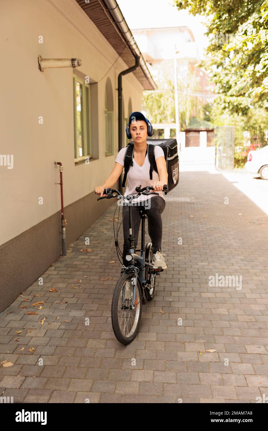 Takeaway food courier in headphones delivering order by bike, front ...
