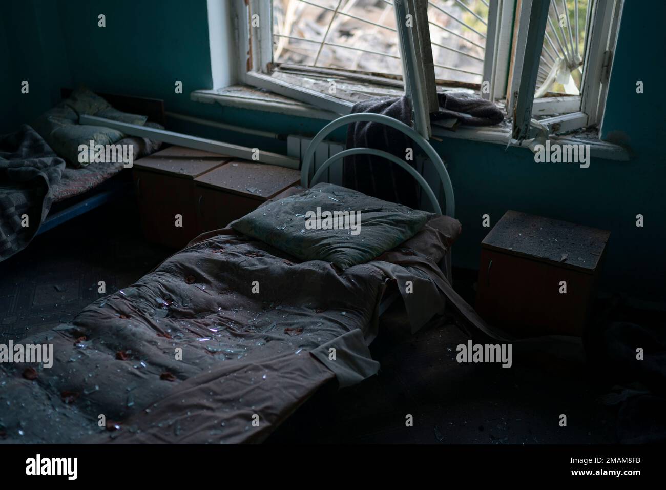 A bed is seen covered with shattered glass from a broken window of a ...