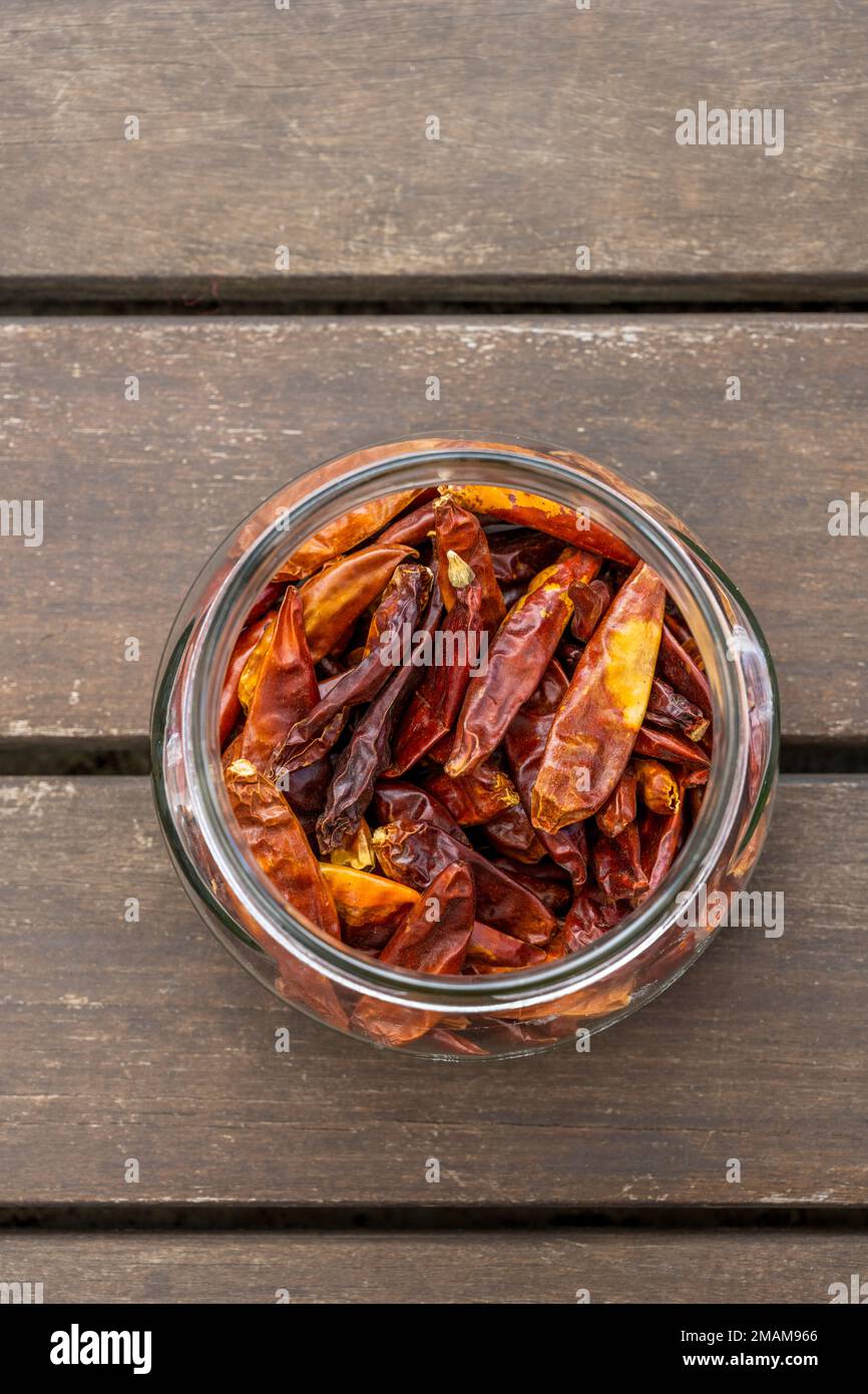 A clear glass jar without a lid full of dried chillies on an acacia ...