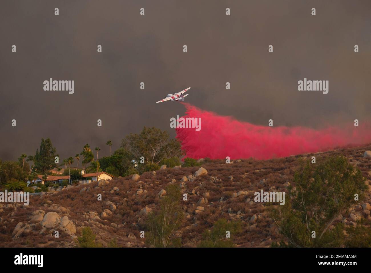 An air tank drops retardant on a wildfire burning behind homes in a ...