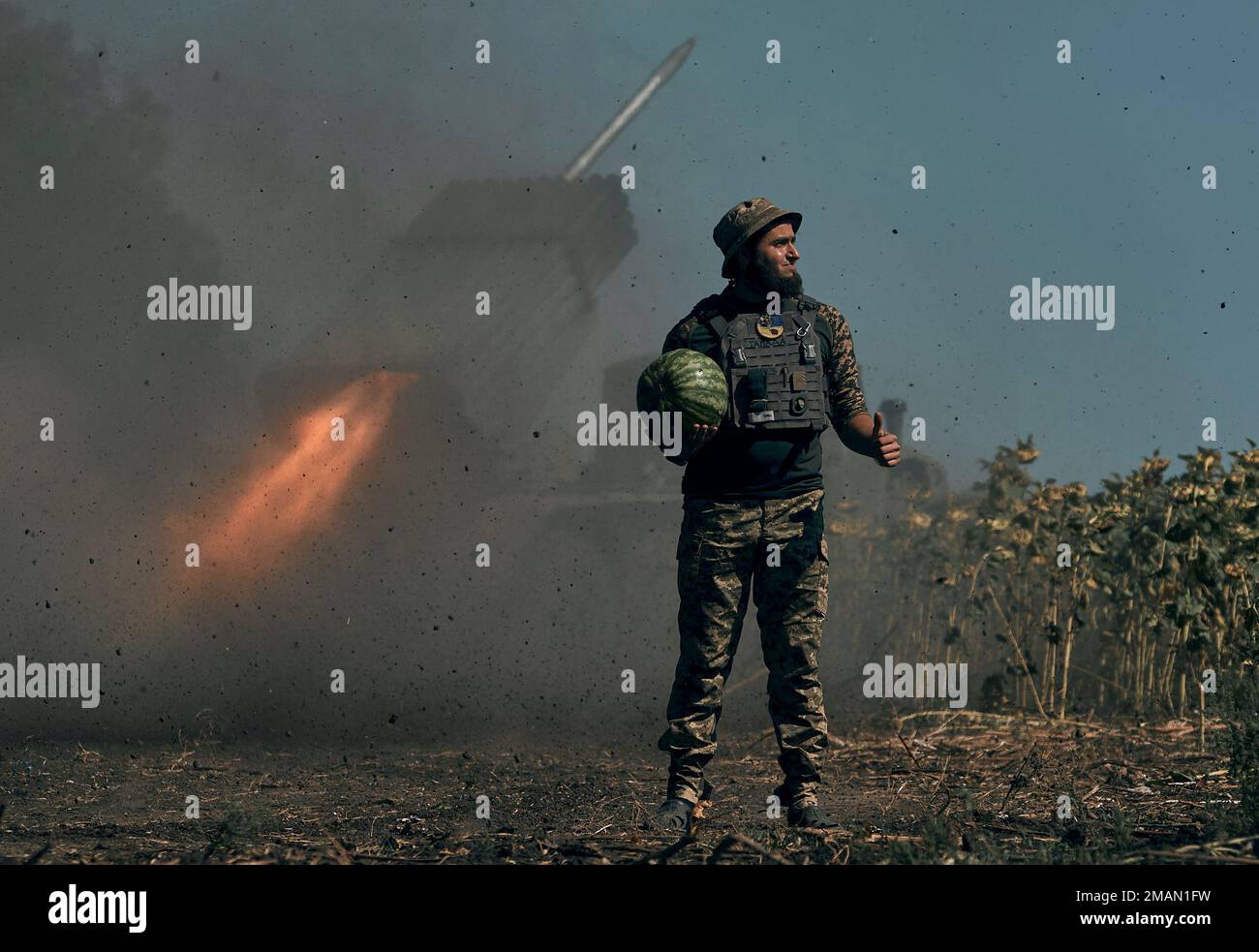 A Ukrainian soldier holds a watermelon and thumbs up as a rocket launch ...
