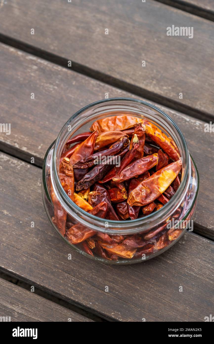 A clear glass jar without a lid full of dried chilli peppers on acacia ...