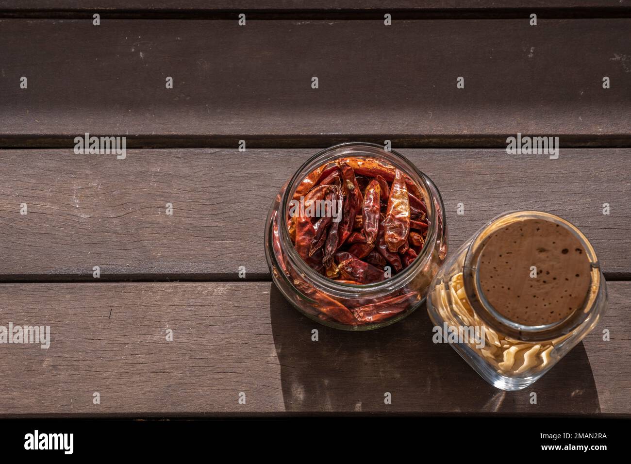 A clear glass jar without a lid filled with dried chillies and another ...