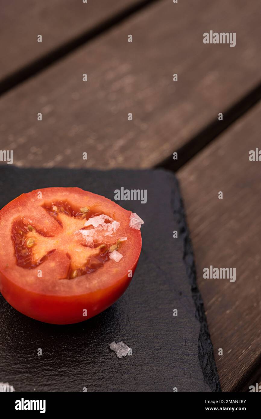 A ripe tomato split in half with sprinkles of coarse salt on a black ...