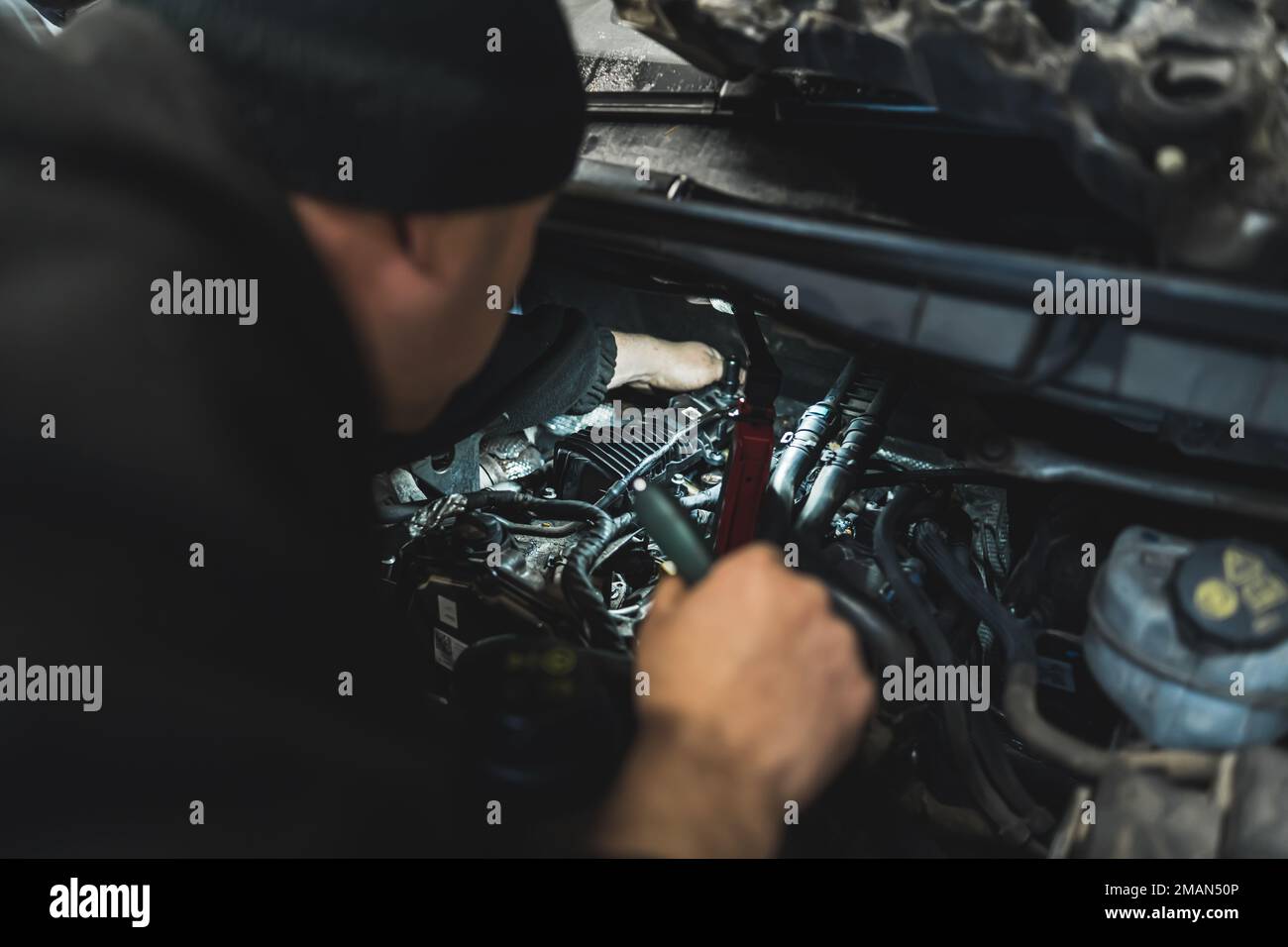A skilled mechanic works diligently on a car with its hood raised to reveal the engine. High ...