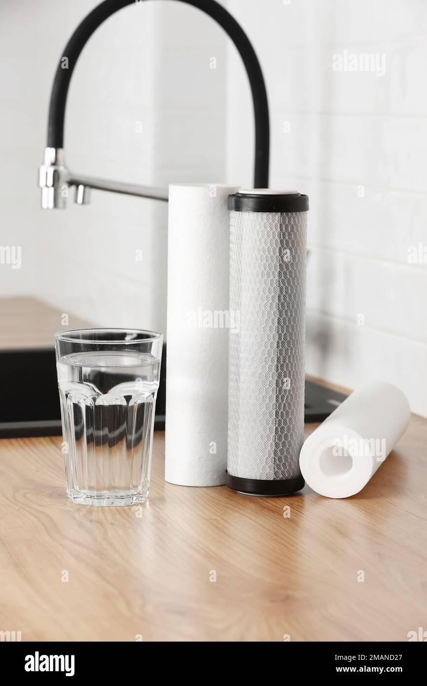 A glass of clean fresh water and set of filter cartridges on wooden ...