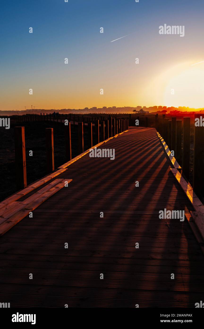 A wooden pathway over a sandy beach leads into the sunset and the ...