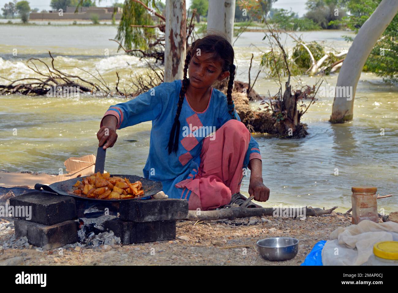 A displaced girl cooks potatoes next to floodwaters after taking refuge ...