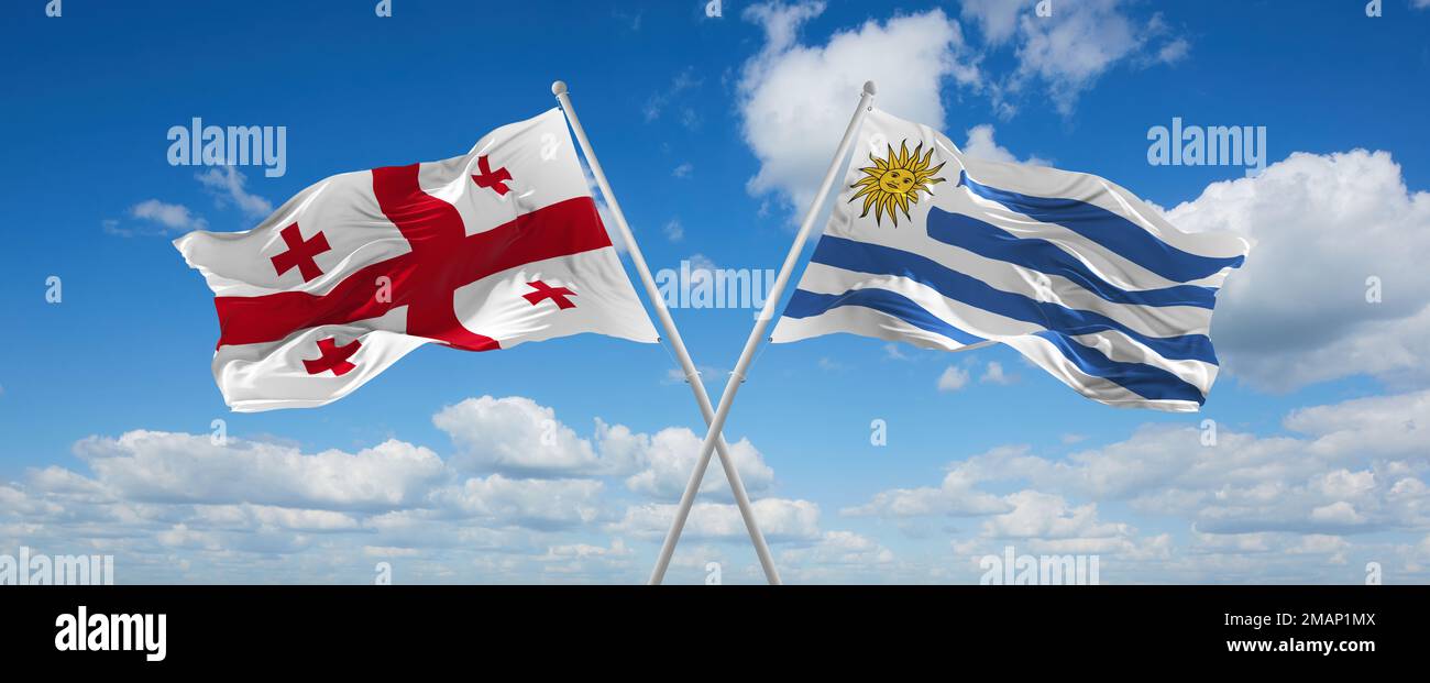two crossed flags Uruguay and Georgia waving in wind at cloudy sky ...