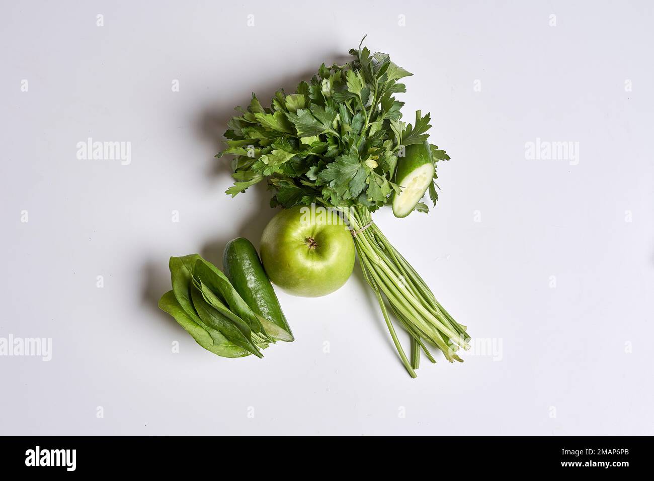 some green vegetables on a white surface with an apple and celery in ...