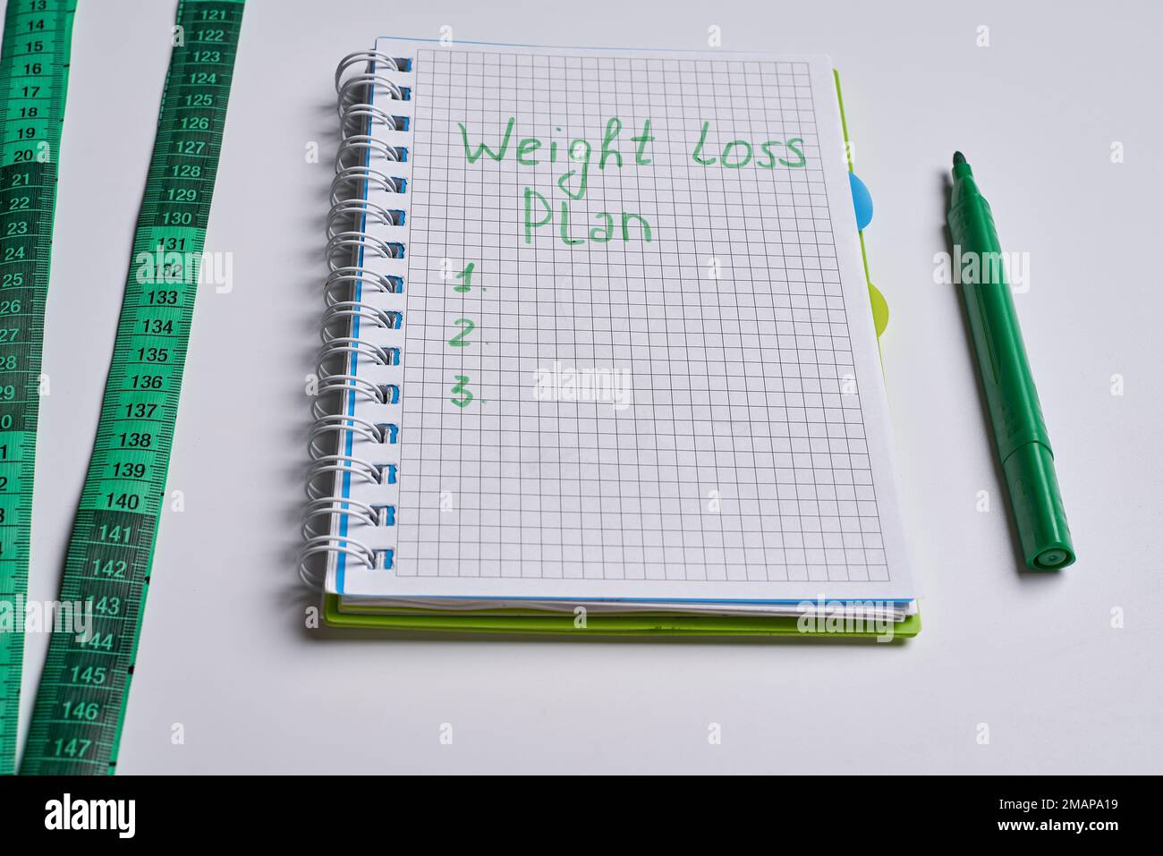 an open notebook with a green pen next to it and a measuring tape on ...