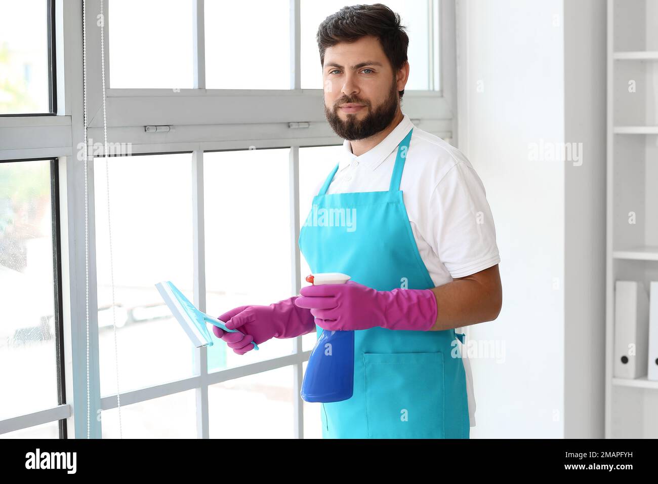 Male janitor with squeegee and detergent near window in office Stock ...