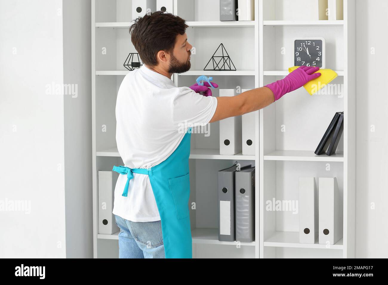 Male janitor cleaning shelving unit in office Stock Photo - Alamy