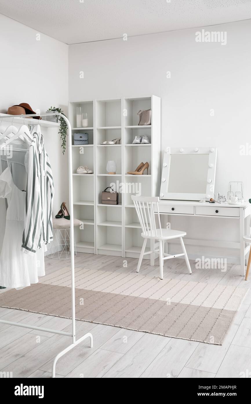 Interior of stylish dressing room with table, shelving unit and clothes ...