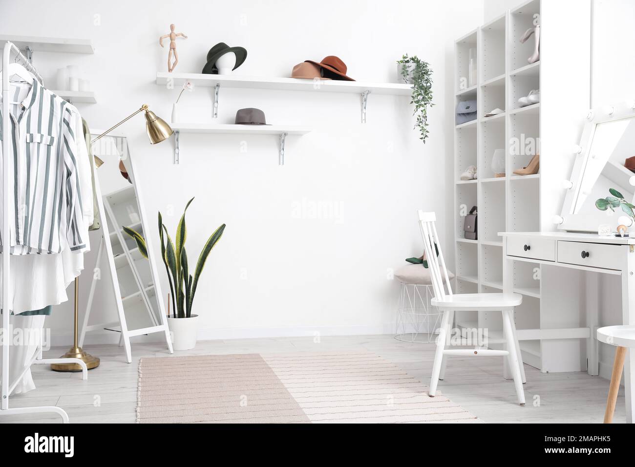 Interior of stylish dressing room with table, shelving unit and clothes ...