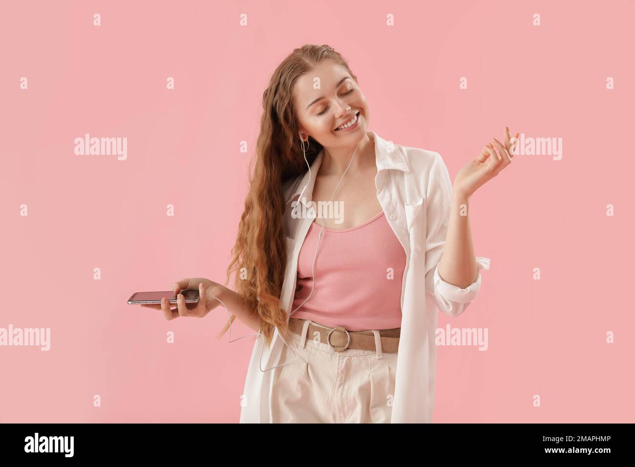 Young woman in earphones with mobile phone listening to music on pink ...