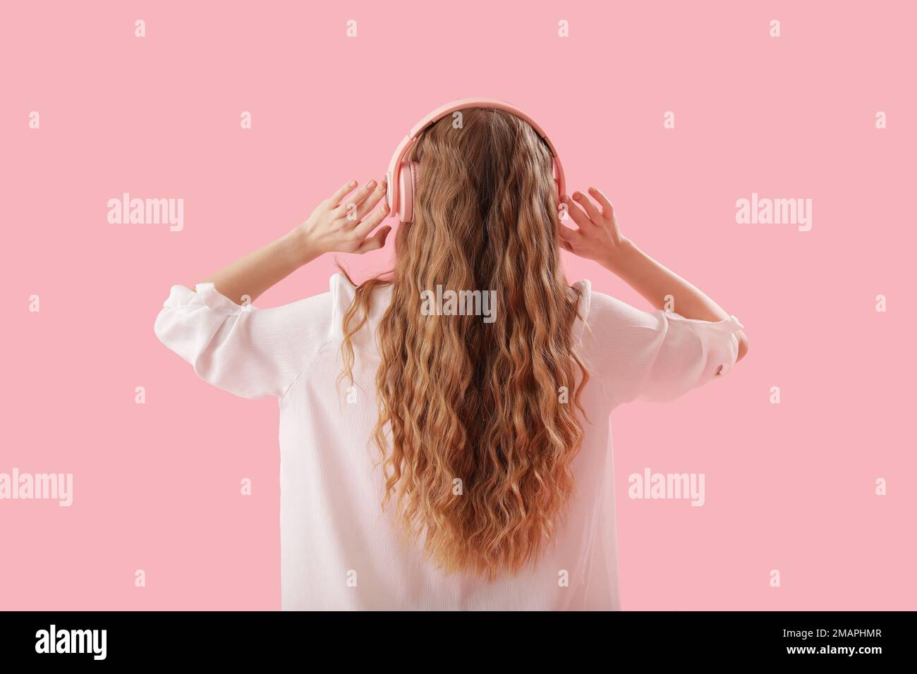 Young woman in headphones listening to music on pink background, back ...