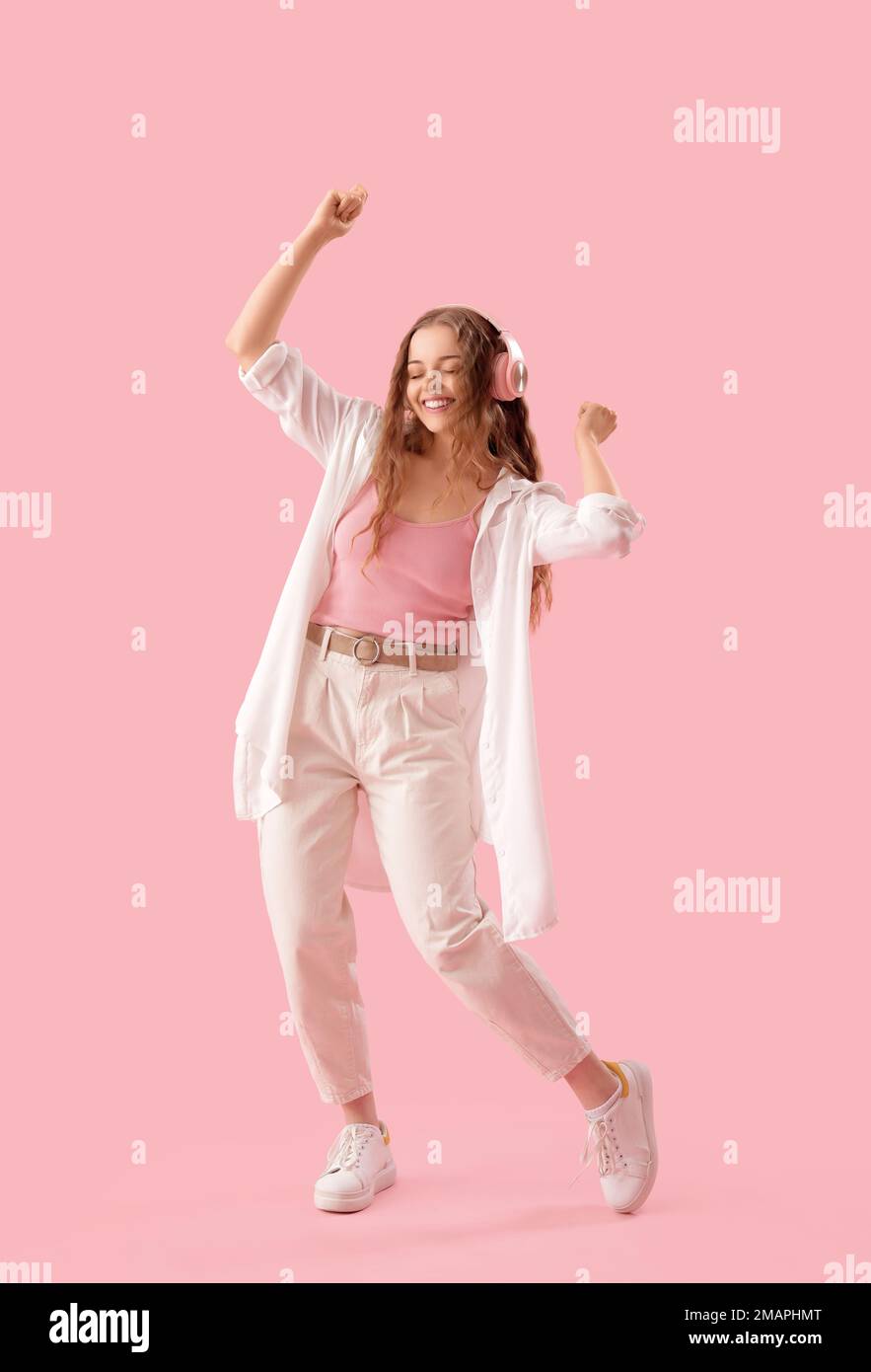 Young woman in headphones dancing on pink background Stock Photo - Alamy