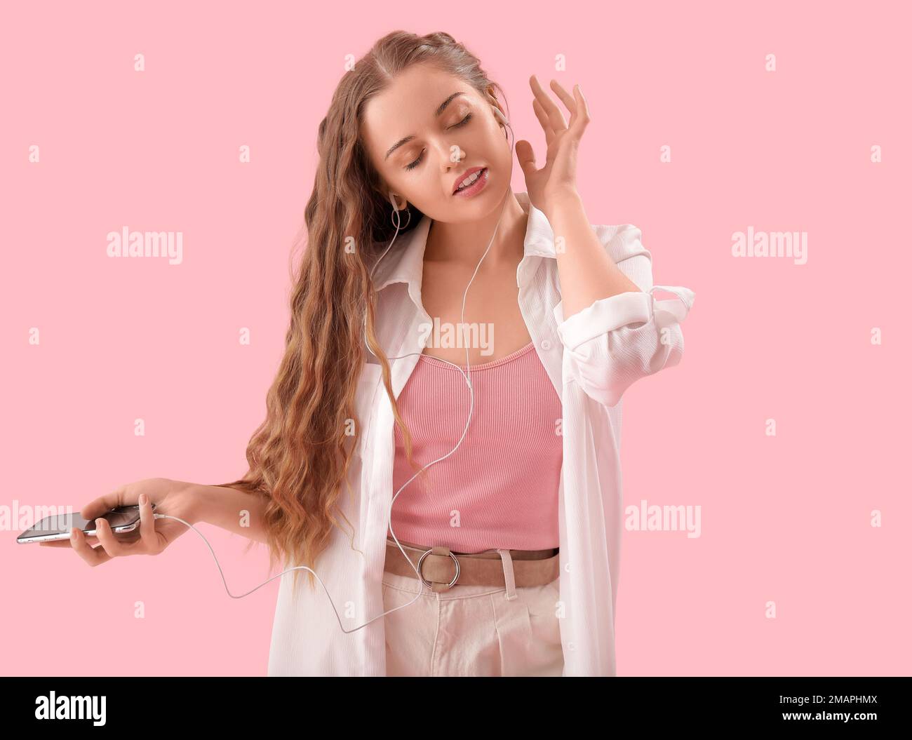 Young woman in earphones with mobile phone listening to music on pink ...