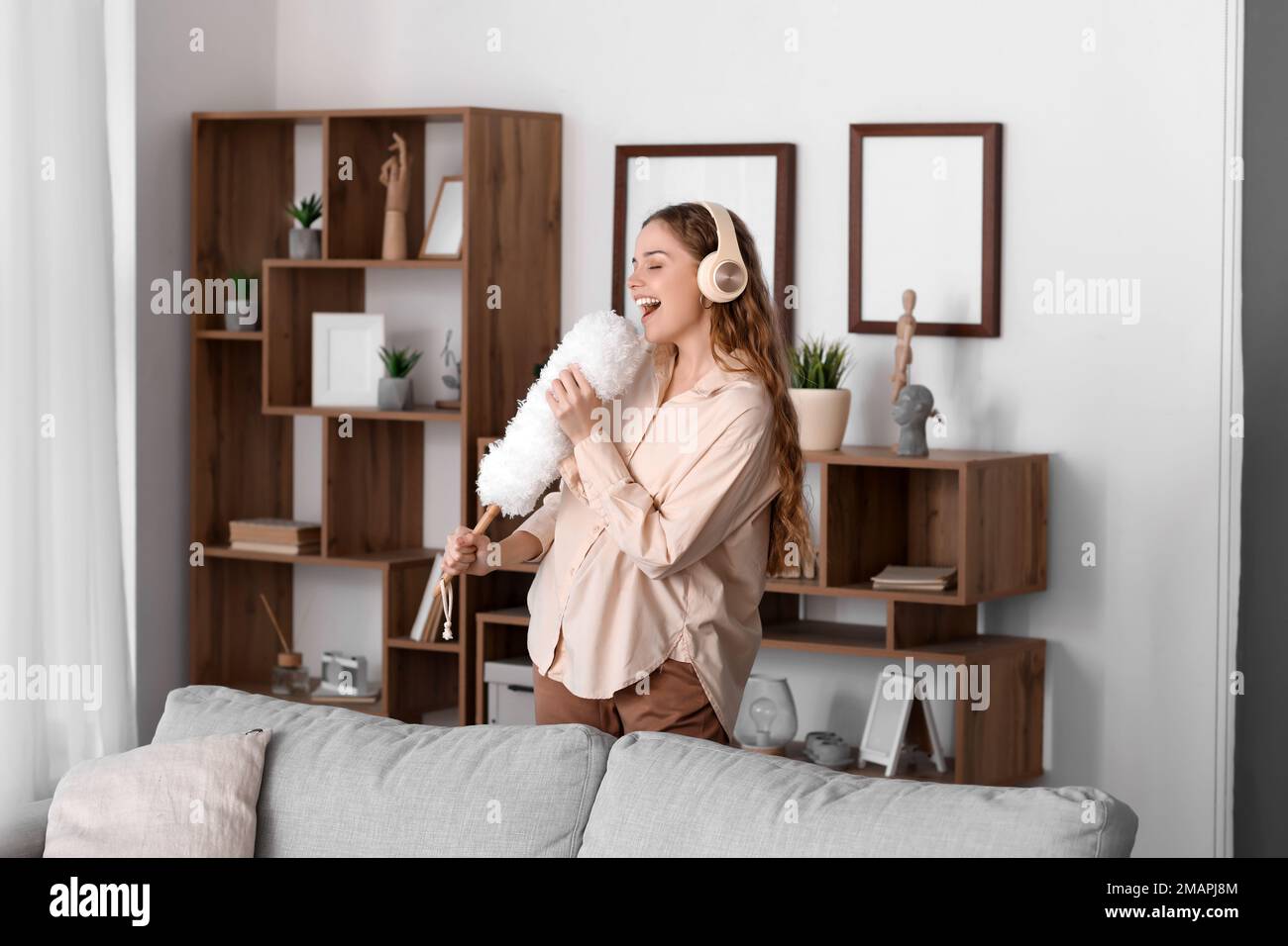 Young woman in headphones with duster singing at home Stock Photo - Alamy