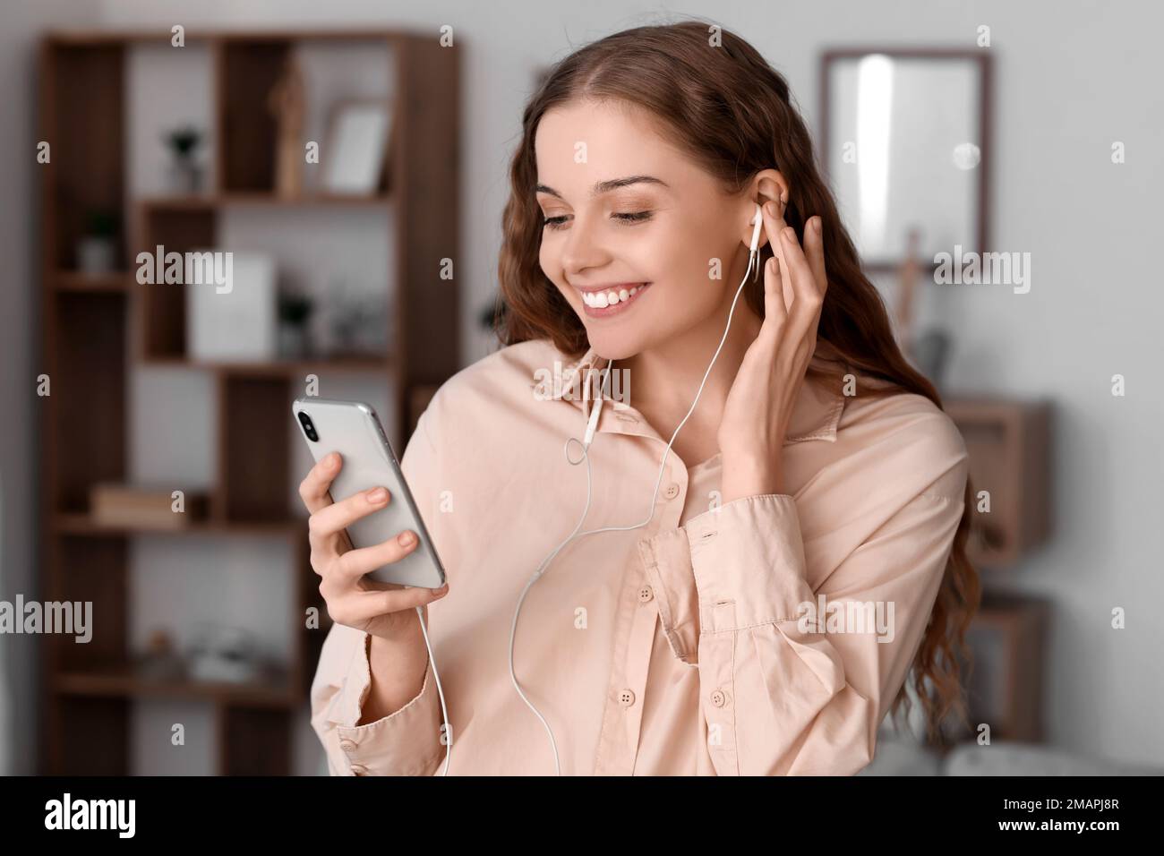 Young woman in earphones with mobile phone listening to music at home ...