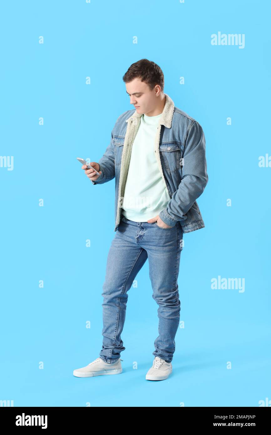 Young man in denim jacket using mobile phone on blue background Stock ...
