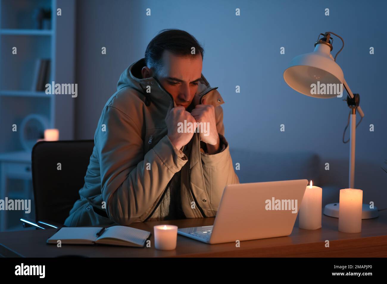 Frozen young man sitting at workplace in office during blackout Stock ...