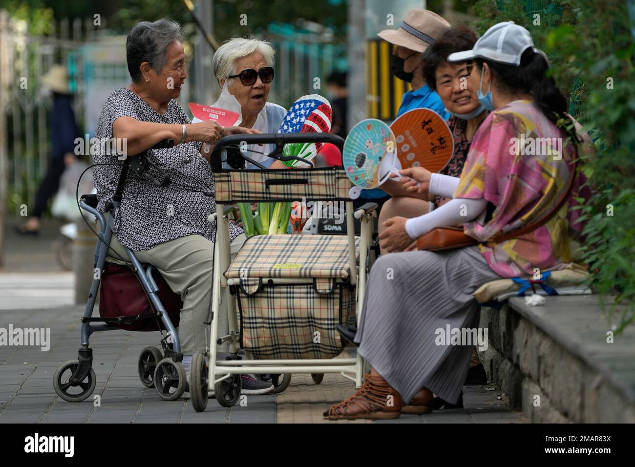 Residents fan themselves as they chat with each other outside a ...