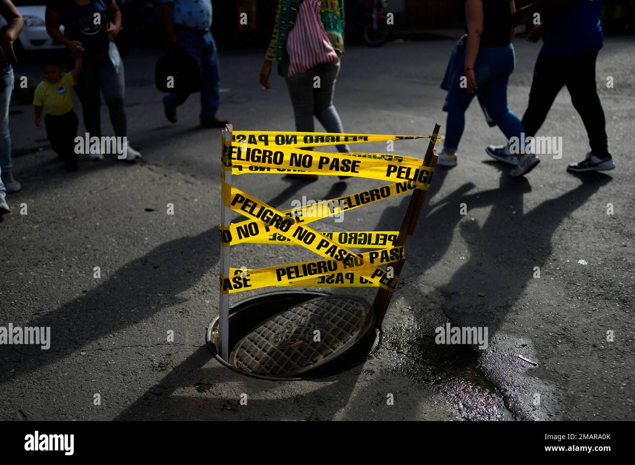Pedestrians walk past a damaged manhole, where two sticks wrapped in ...