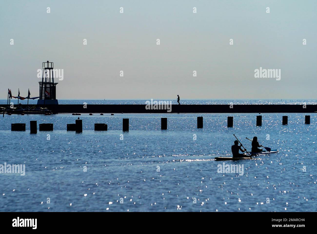 Kayakers and a runner are silhouetted against the morning sunlight at ...