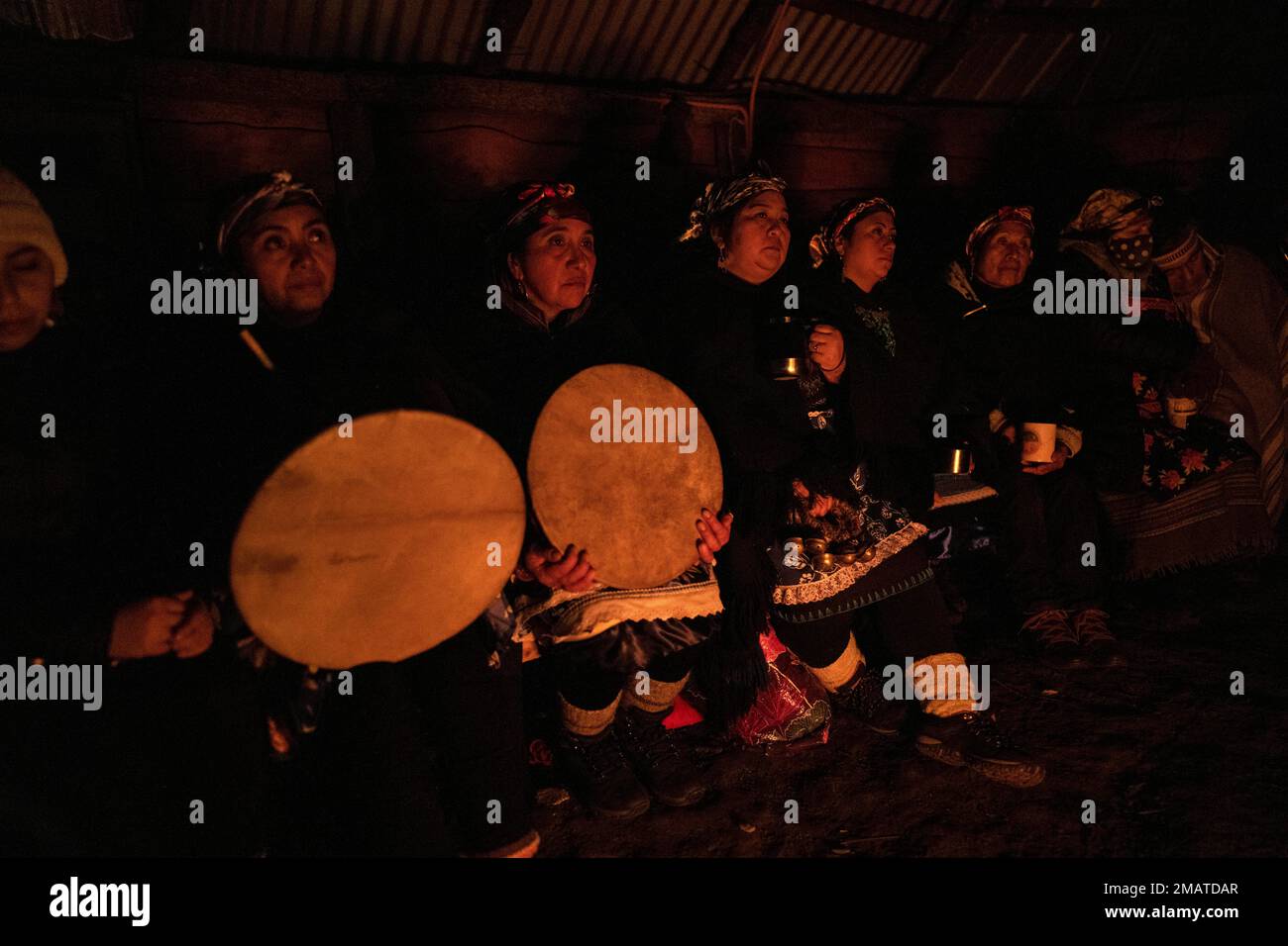 Mapuche gather round a campfire, some holding ceremonial drums inside a ...
