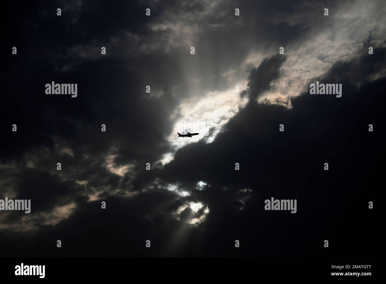 A passenger plane flies underneath dark clouds illuminated by some sun ...