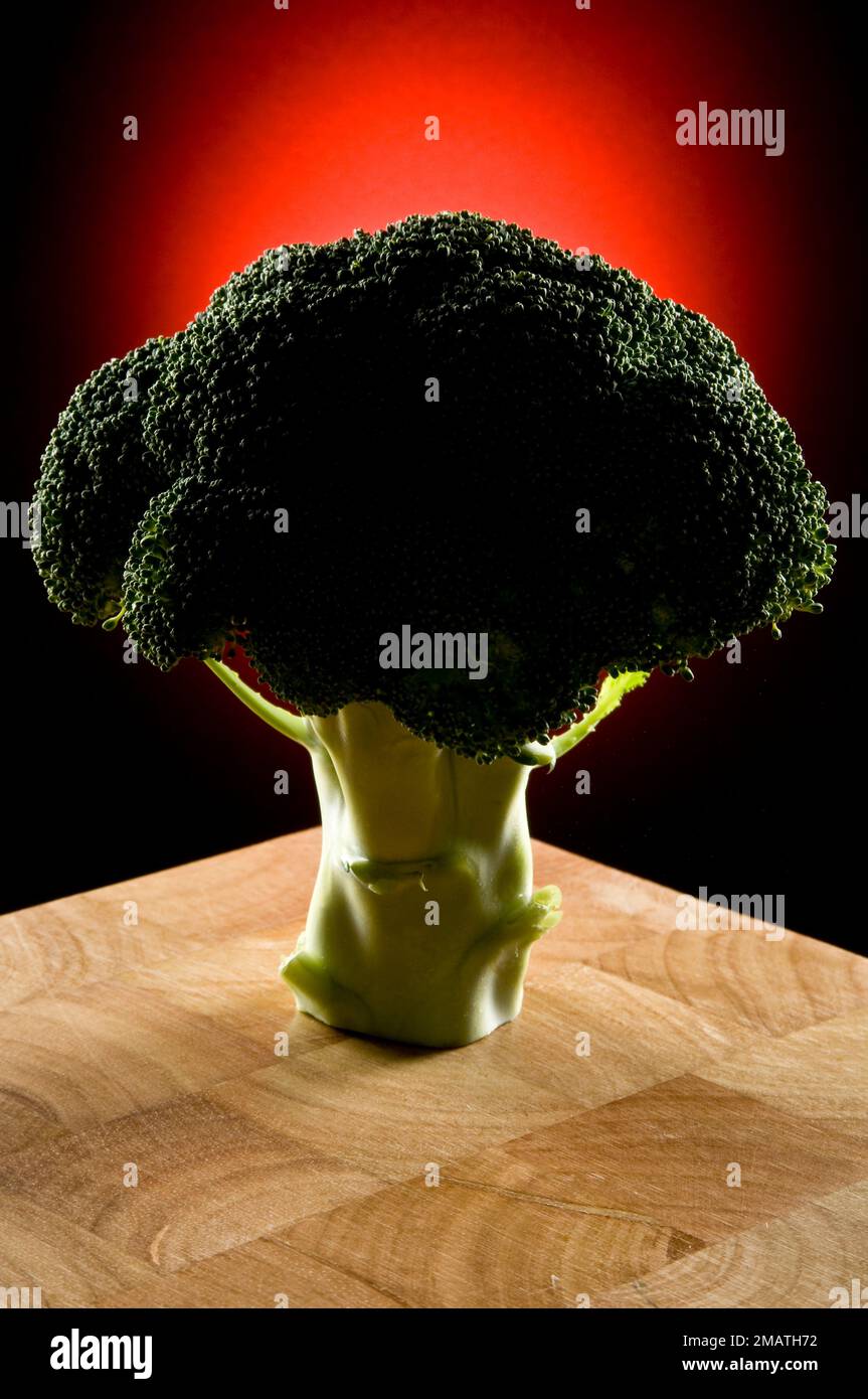Whole broccoli head on timber bench low key side lit with green spot on ...