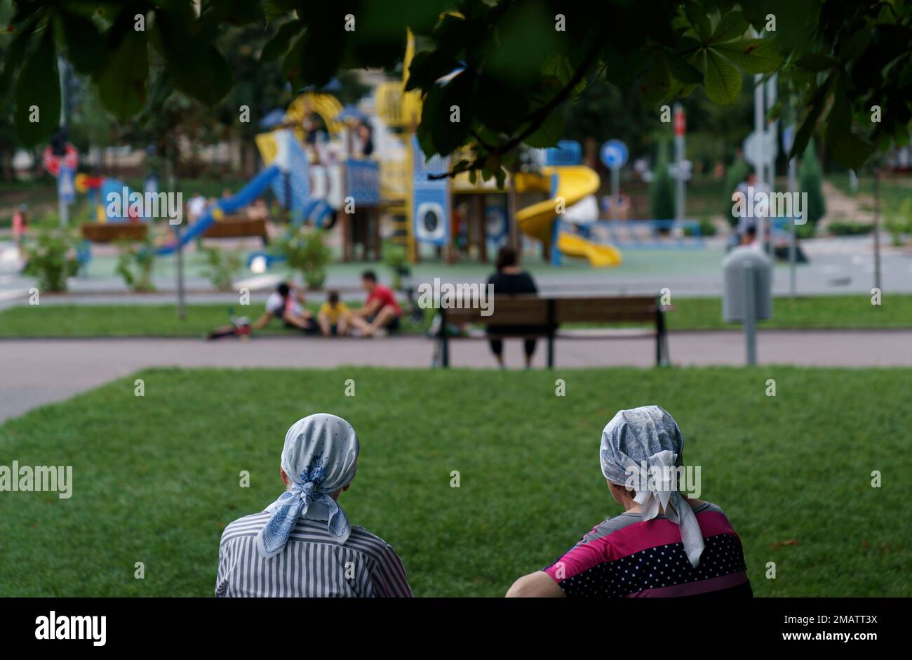 Two elderly women sit on a park bench overlooking a playground in ...