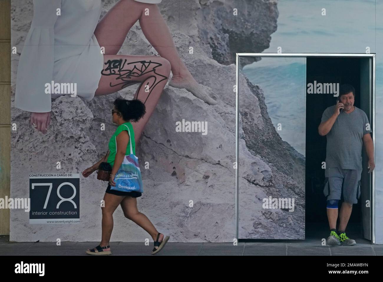 A man speaks on his phone as a woman walks by an advertising poster in ...