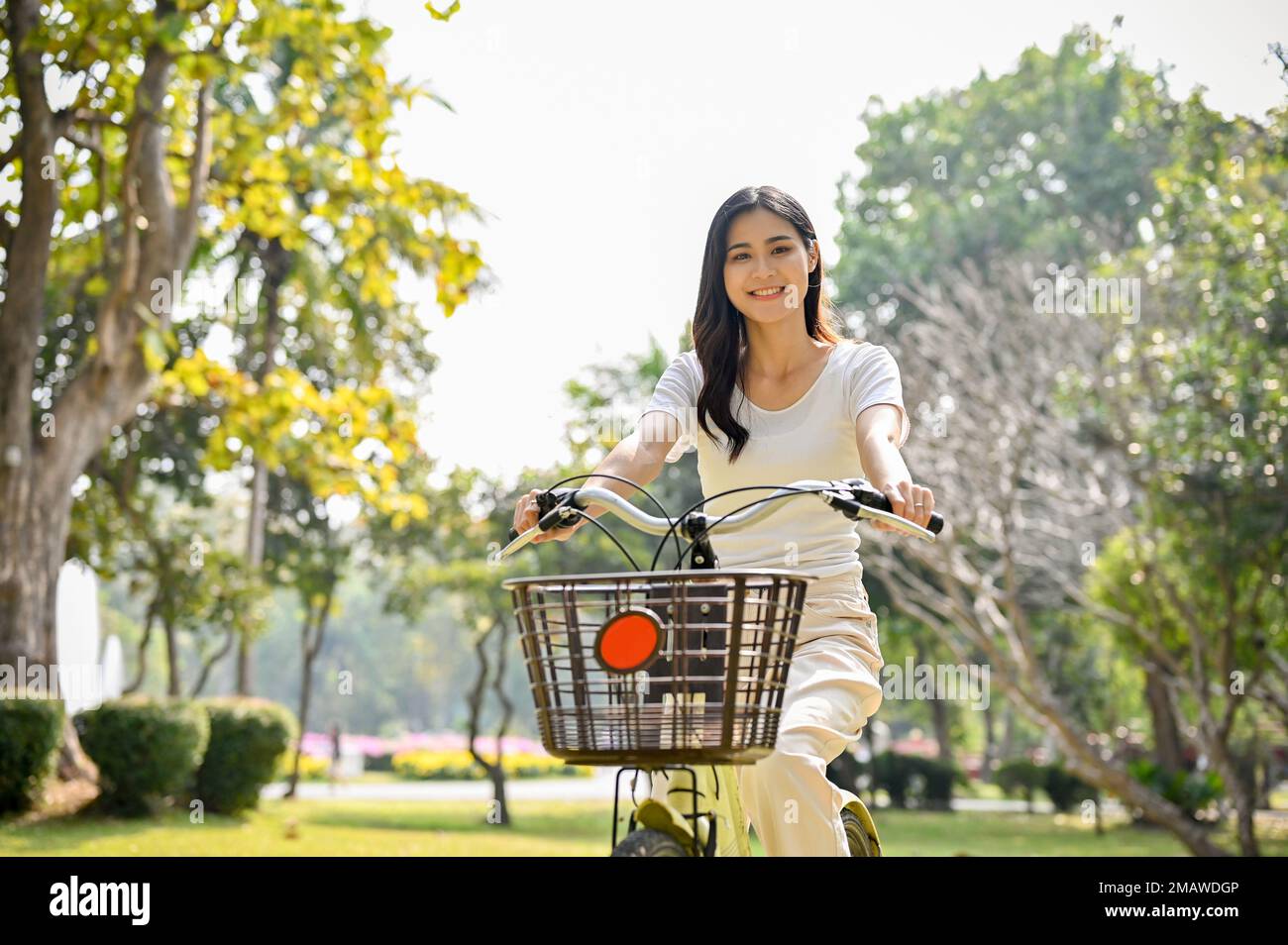 Charming and chill young Asian woman in casual clothes riding a bike in the beautiful public ...