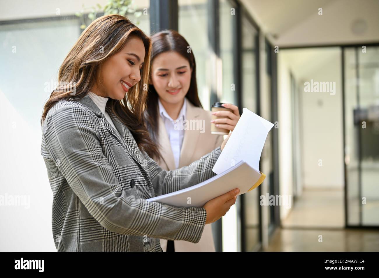 Happy and satisfied millennial Asian female boss standing by the window ...