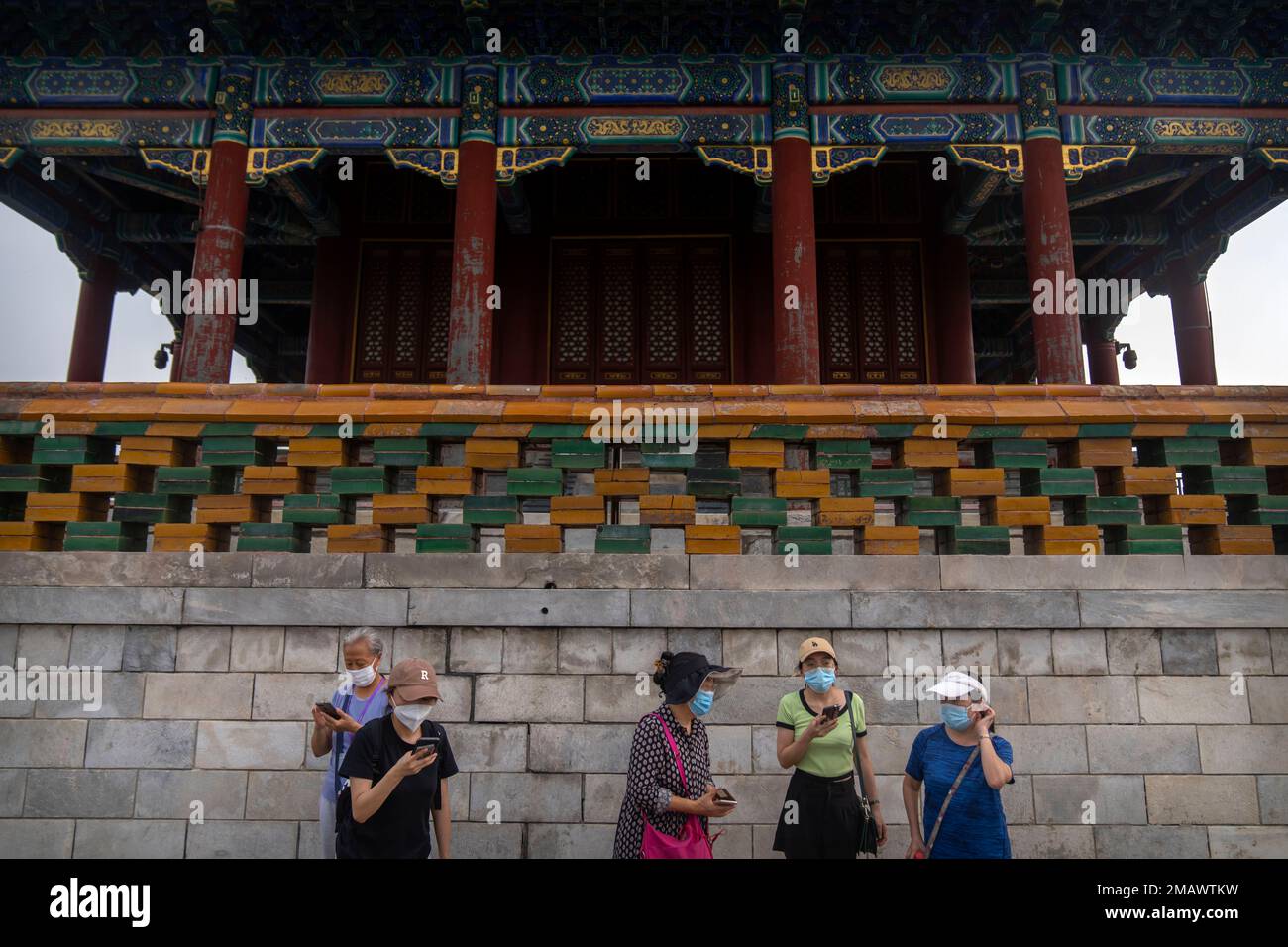 Visitors wearing face masks stand alongside a pavilion at a public park ...