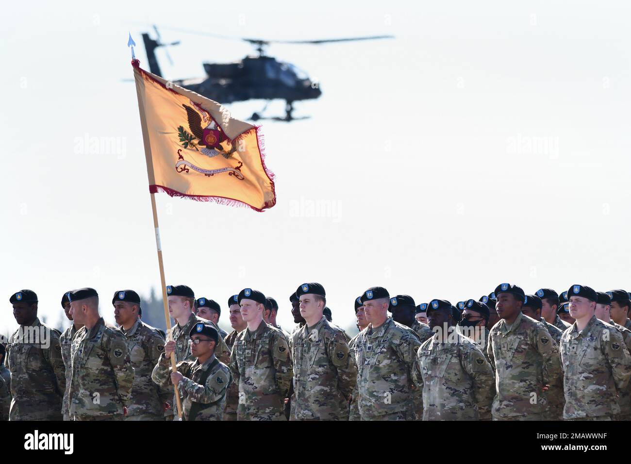 Soldiers stand in formation as an AH-64 Apache helicopter flies ...