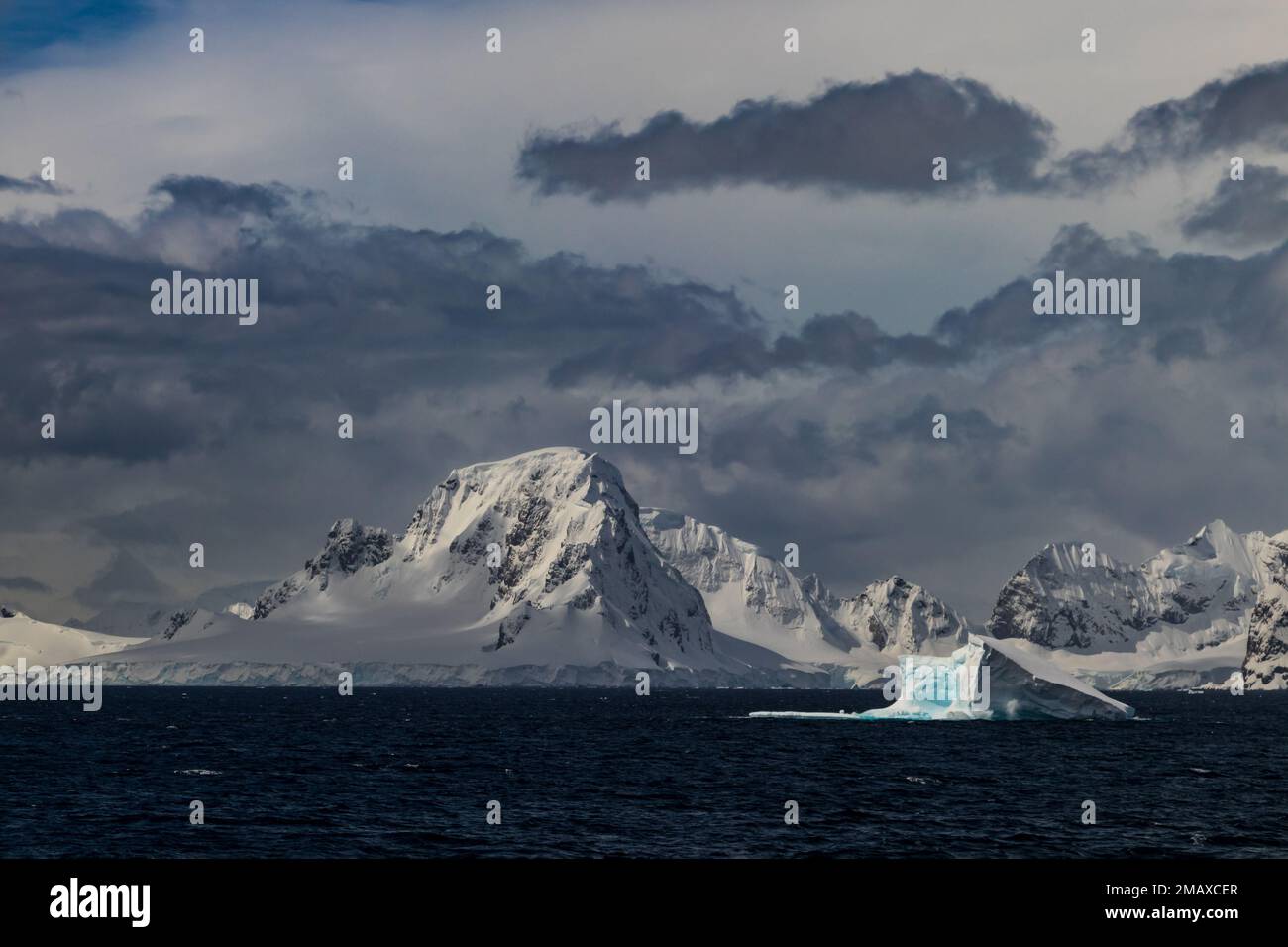 Jagged mountains on Antarctic Peninsula. Small iceberg with bright blue ...