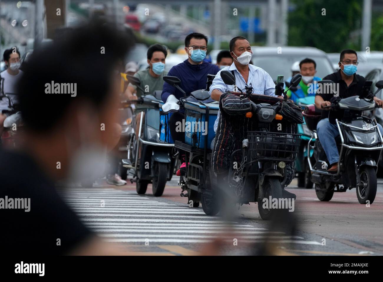 People wearing face masks ride electric bikes, crossing a traffic ...