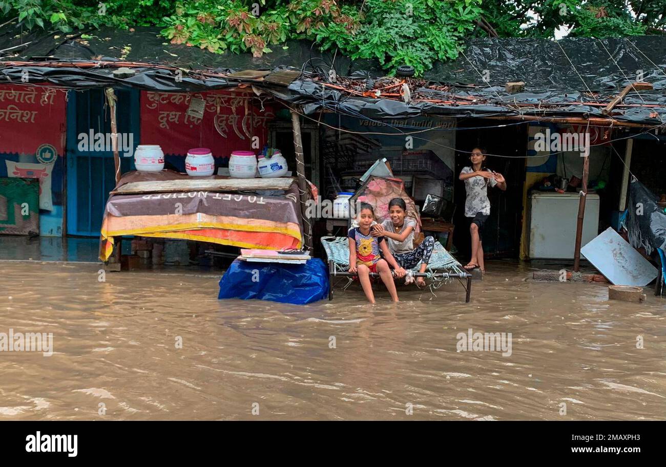 Children sitting outside flooded shanties react to camera as heavy rain ...
