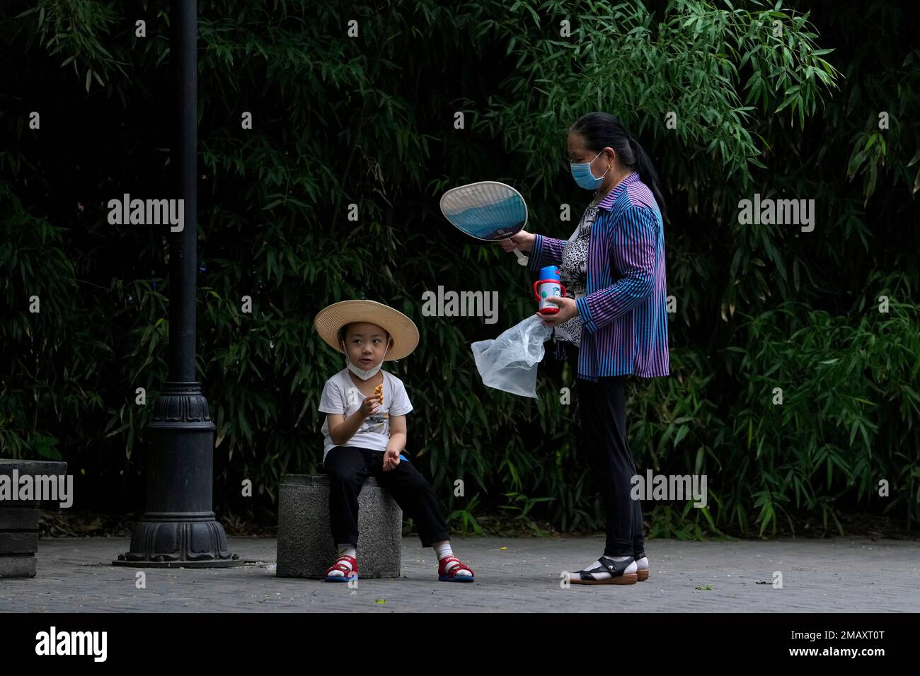 A woman wearing a face mask fans a child eating a snack at a green ...