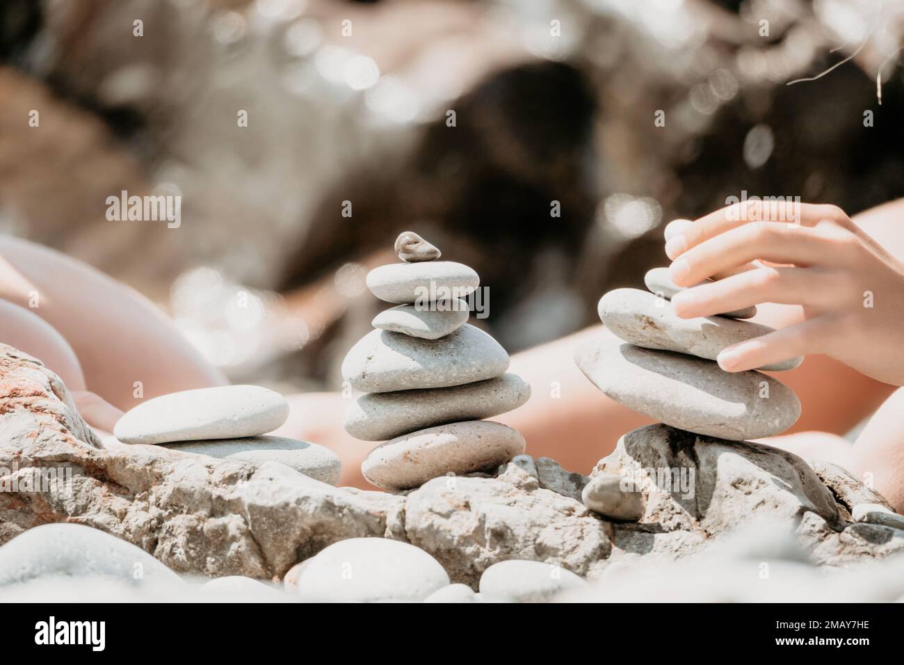 Woman with daughter bilds stones pyramid on seashore on a sunny day on ...