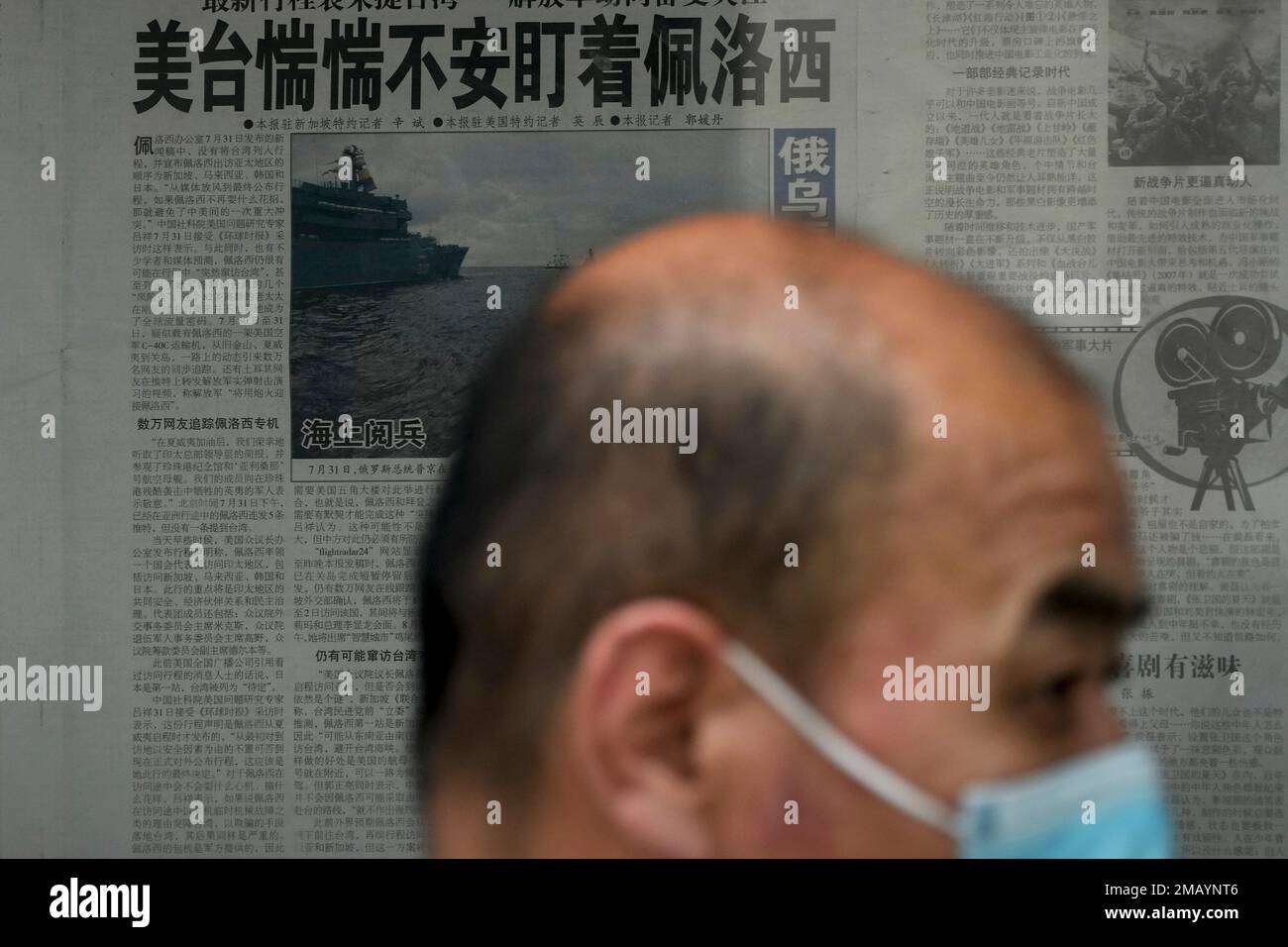 A man wearing a face mask stands in front of a newspaper headline ...