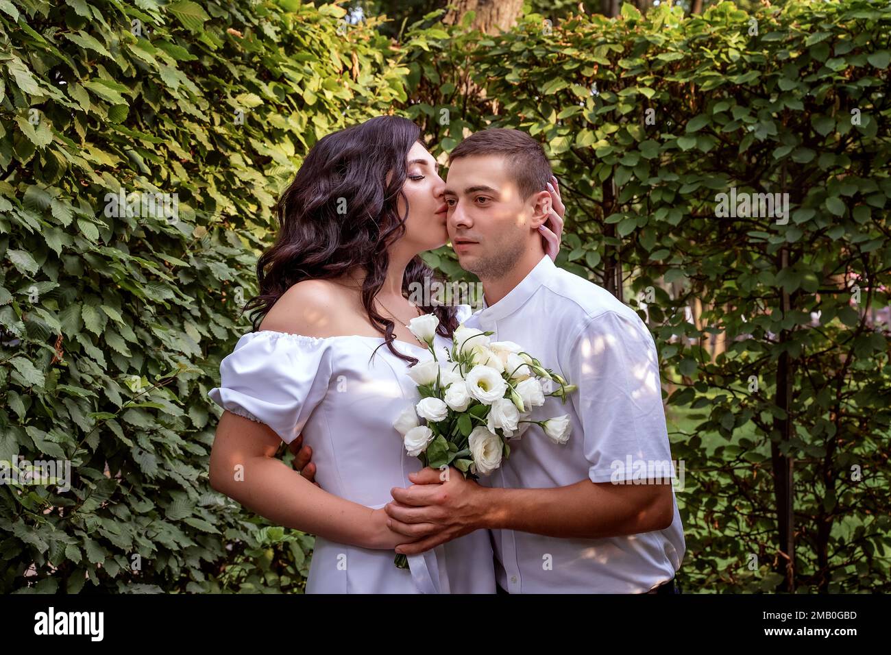 Girl in white dress gently hugs her boyfriend's neck and kisses him on ...