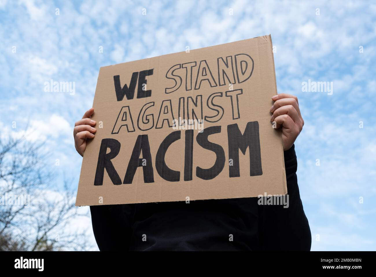 Girl holding a cardboard banner sign with slogan We Stand Against ...